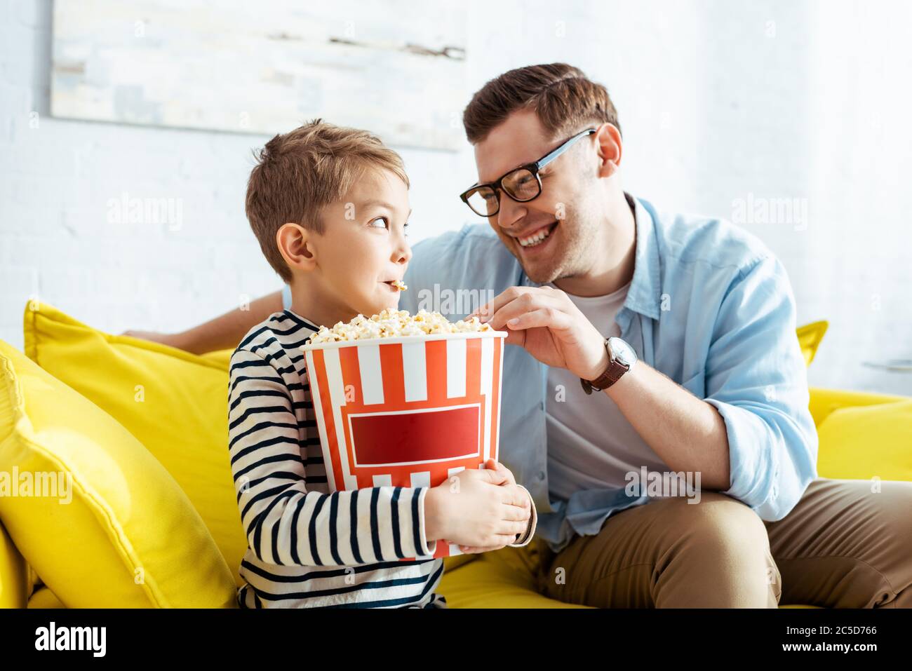 happy father and son looking at each other while eating popcorn from ...