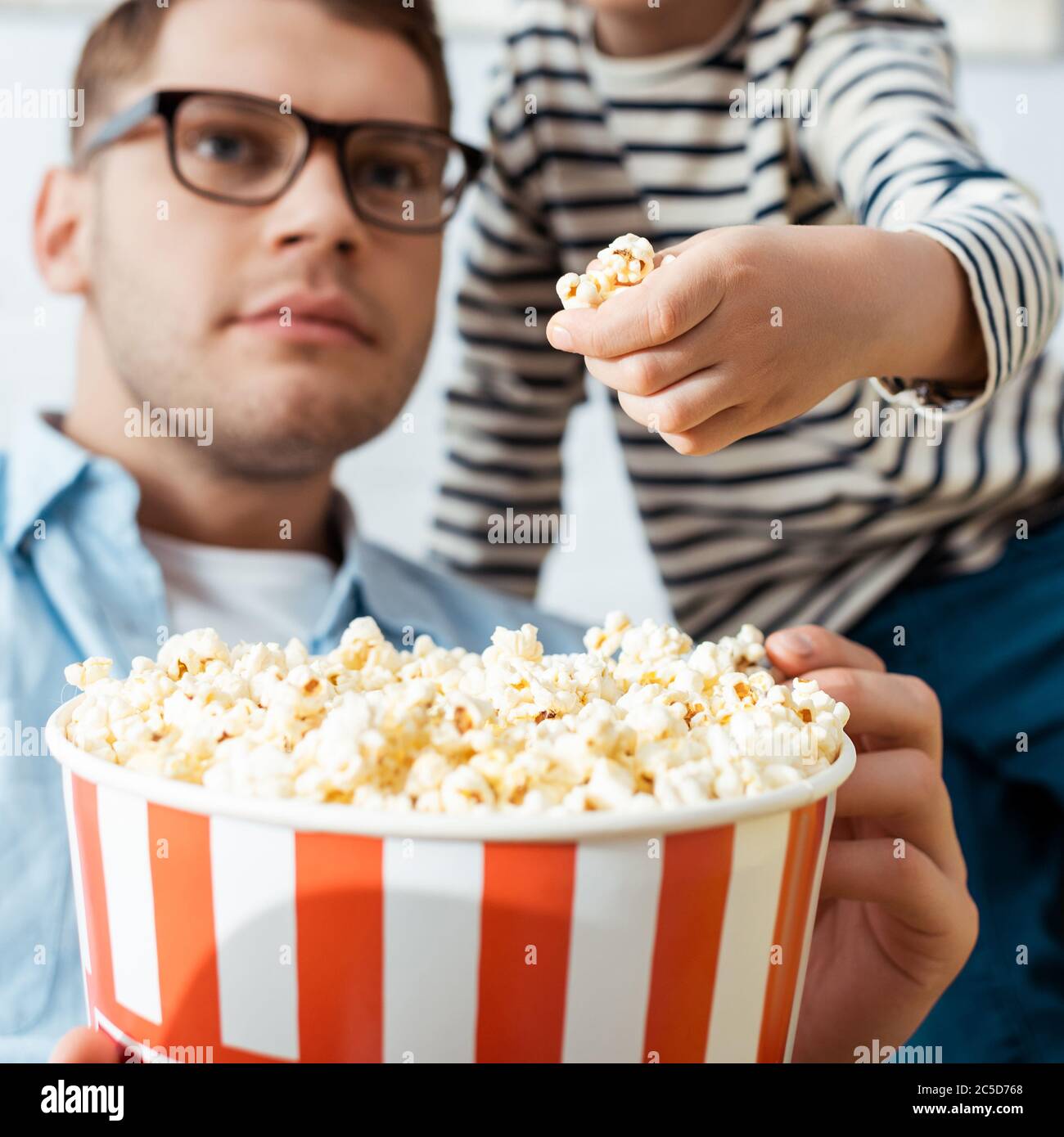 cropped view of boy taking popcorn from bucket while attentive father ...