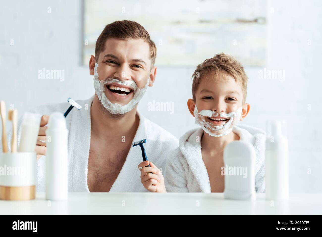 selective focus of cheerful father and son with shaving foam on faces ...