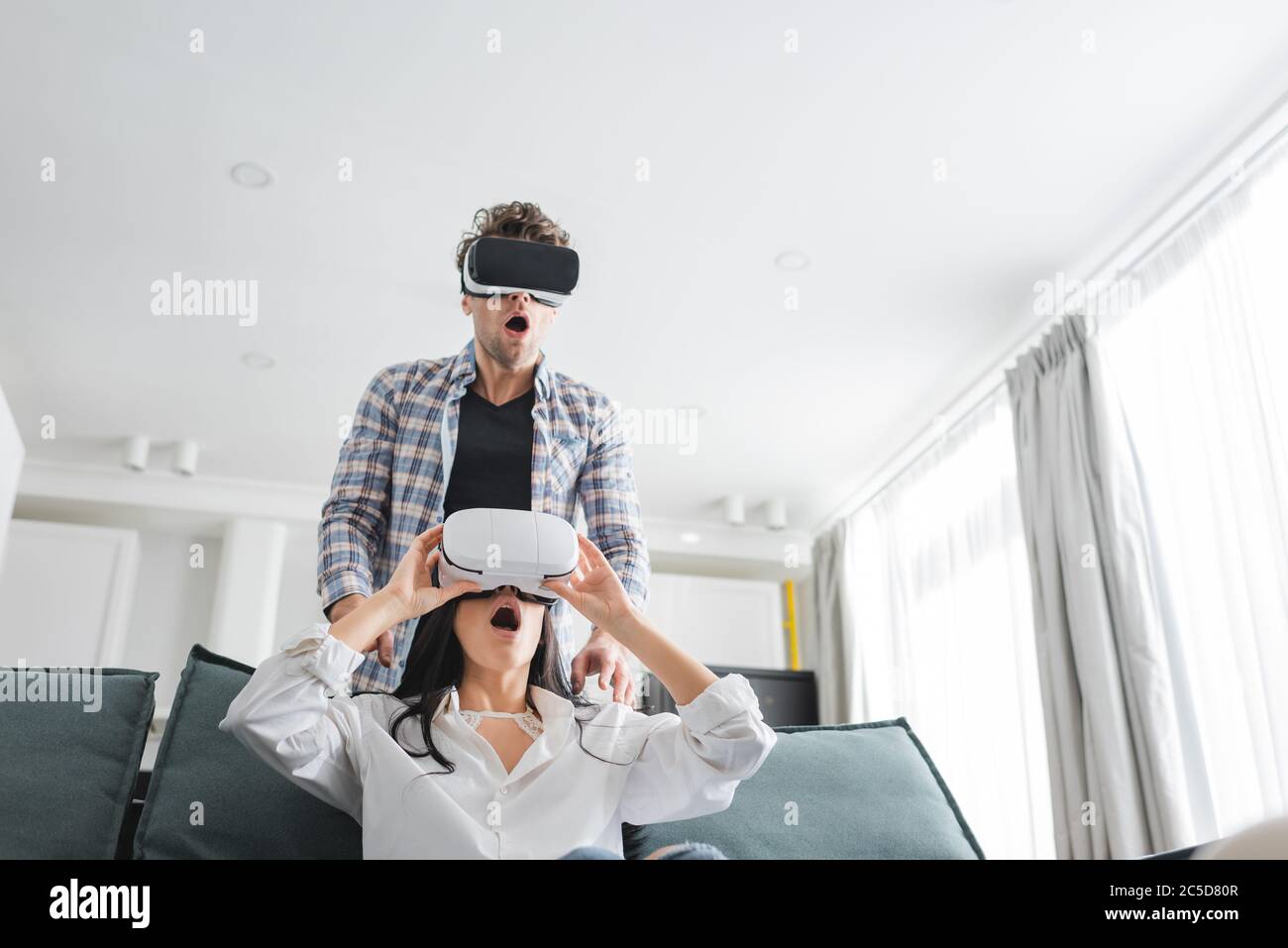 Shocked couple using virtual reality headsets in living room Stock ...