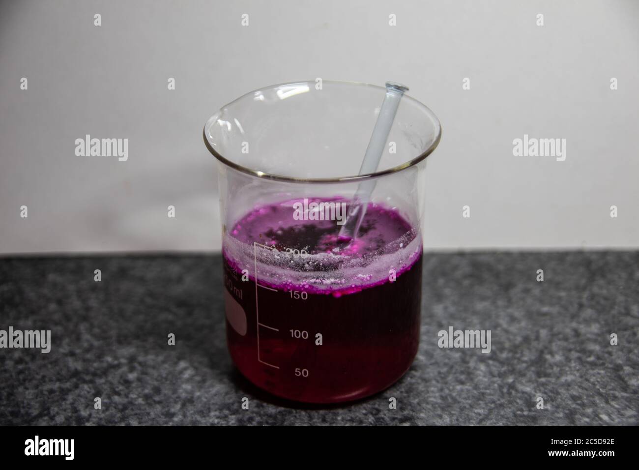 Beaker with liquid is colored dark purple by adding a powder while ...