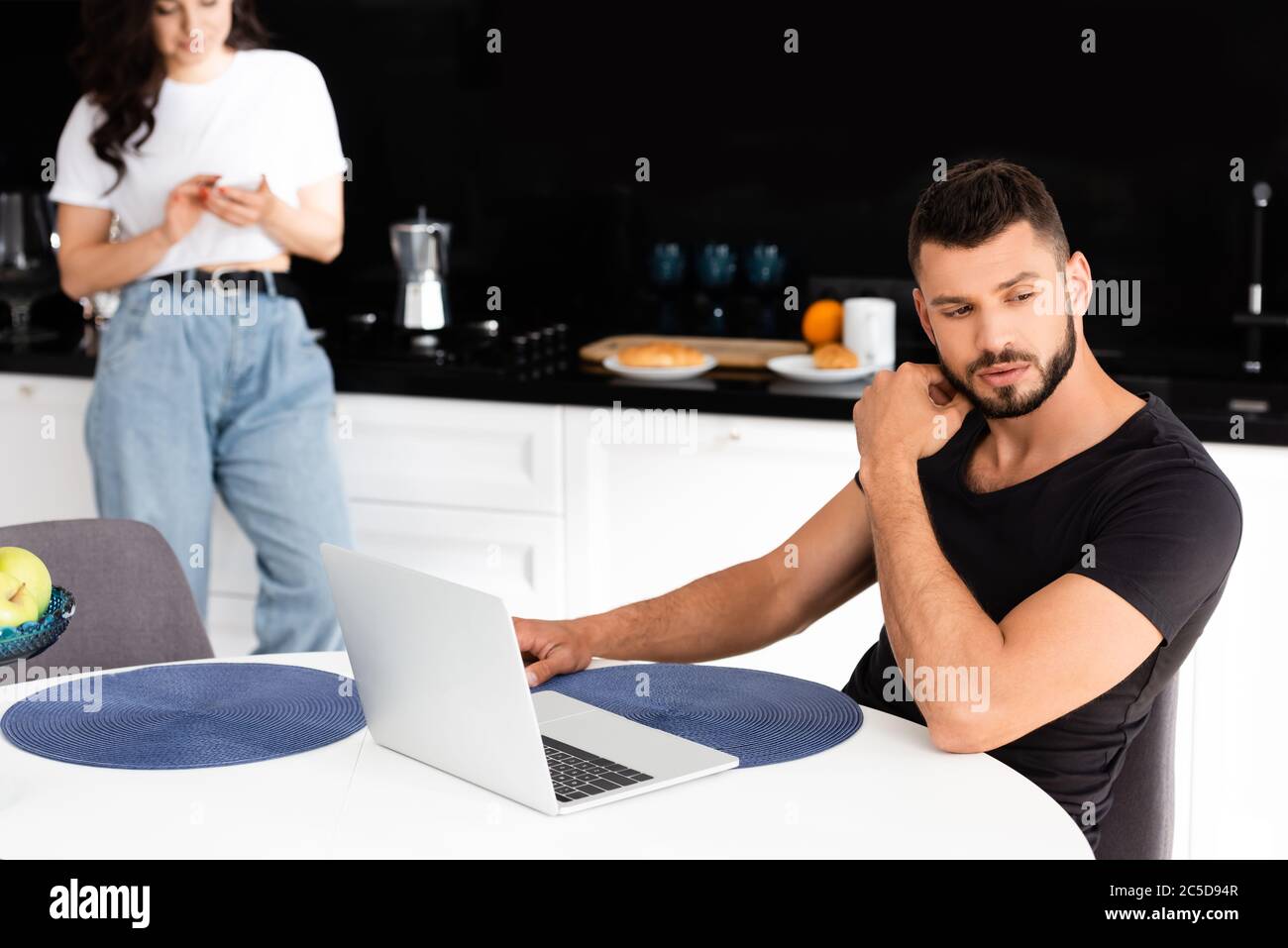selective focus of handsome freelancer looking away near laptop and girl using smartphone Stock ...