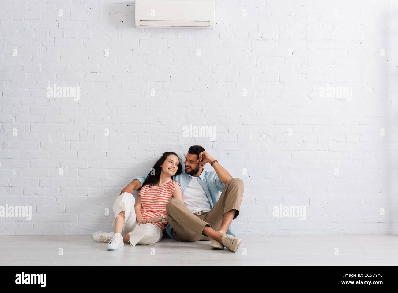 Handsome man embracing beautiful girlfriend while sitting under air ...