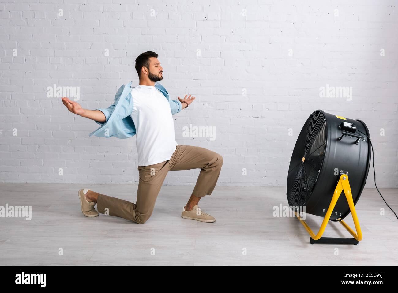 Handsome man standing on knee near electric fan on floor at home Stock ...
