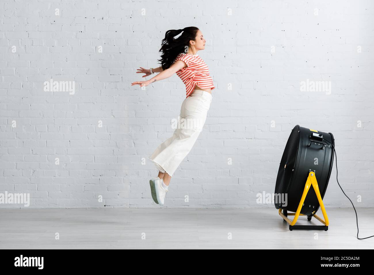 Side view of woman jumping near electric fan at home Stock Photo - Alamy