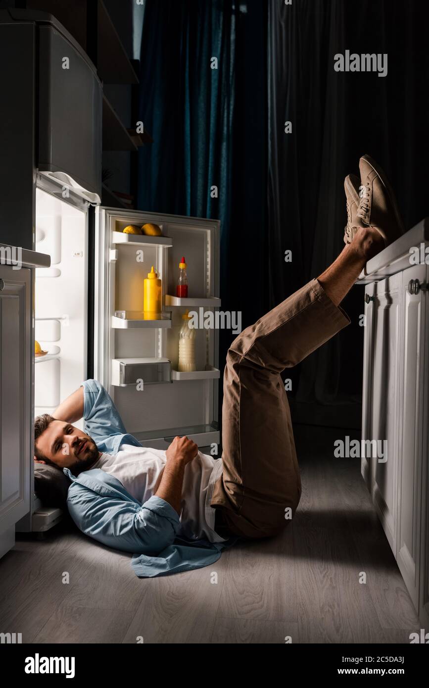 Side view of man looking at camera while lying on floor near open ...