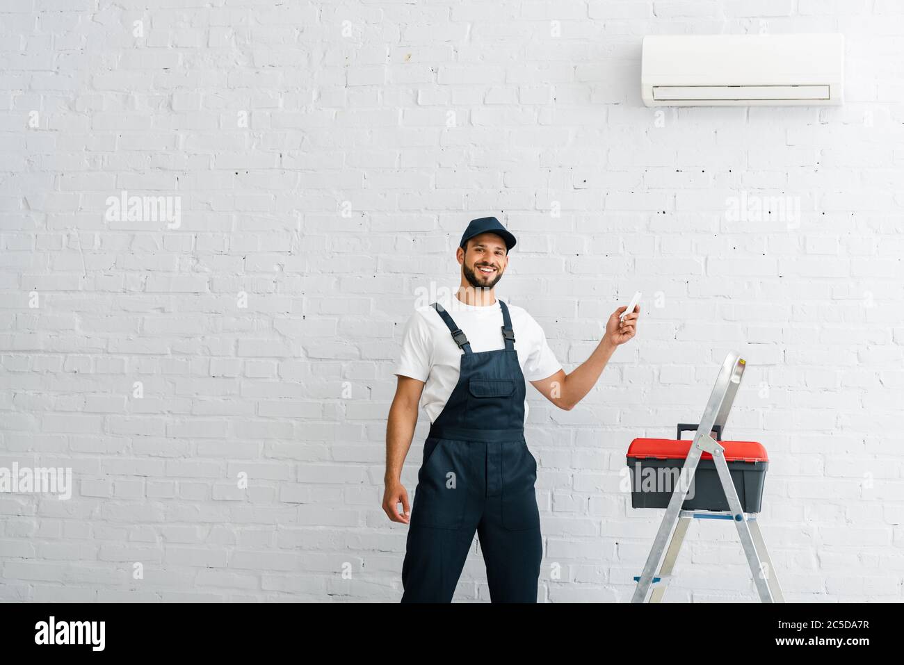 Handsome workman in overalls smiling while holding remote controller of ...