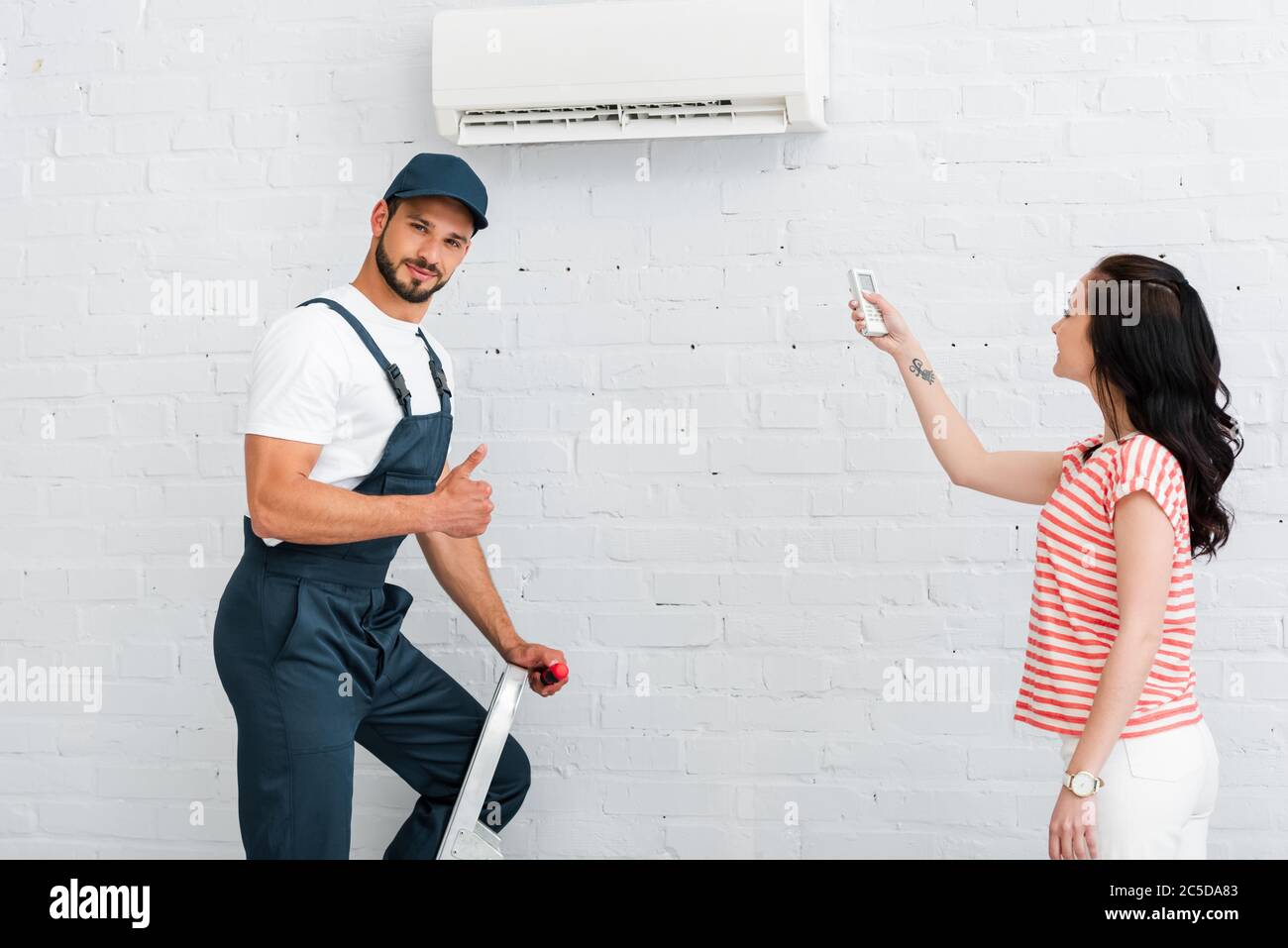 Handsome workman showing thumb up near smiling woman using remote ...