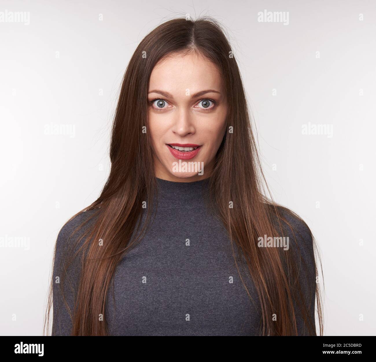 Surprised beautiful woman with long brown hair isolated on grey studio ...