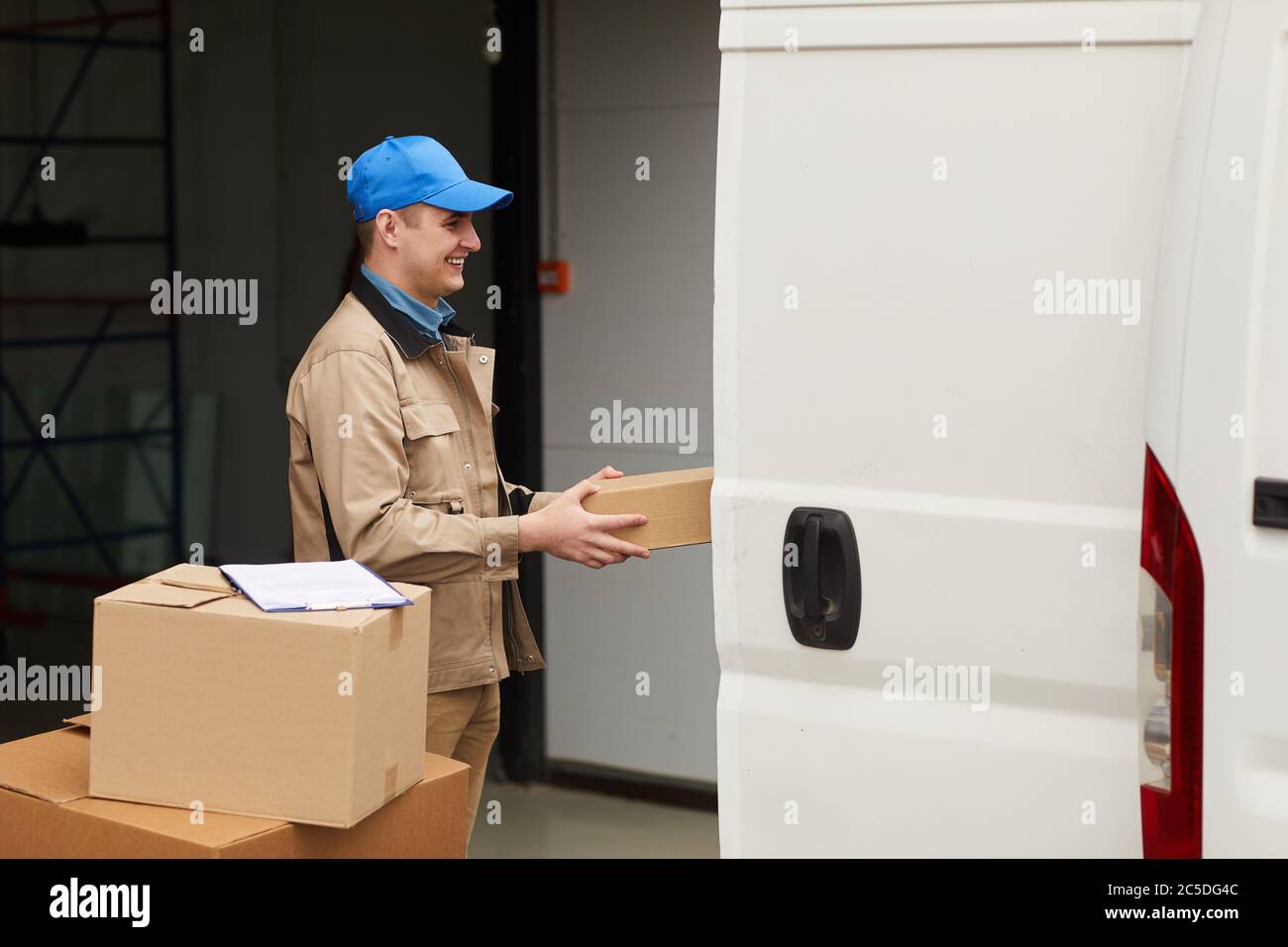 Manual worker carrying boxes and loading them into the van in warehouse ...