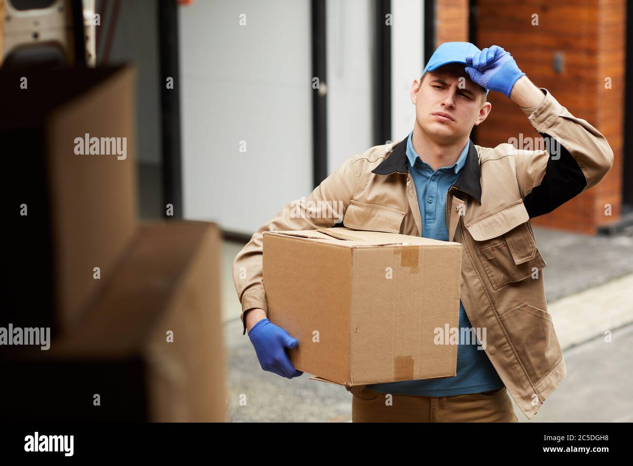 Young man in uniform carrying cardboard box to the van he loading the ...