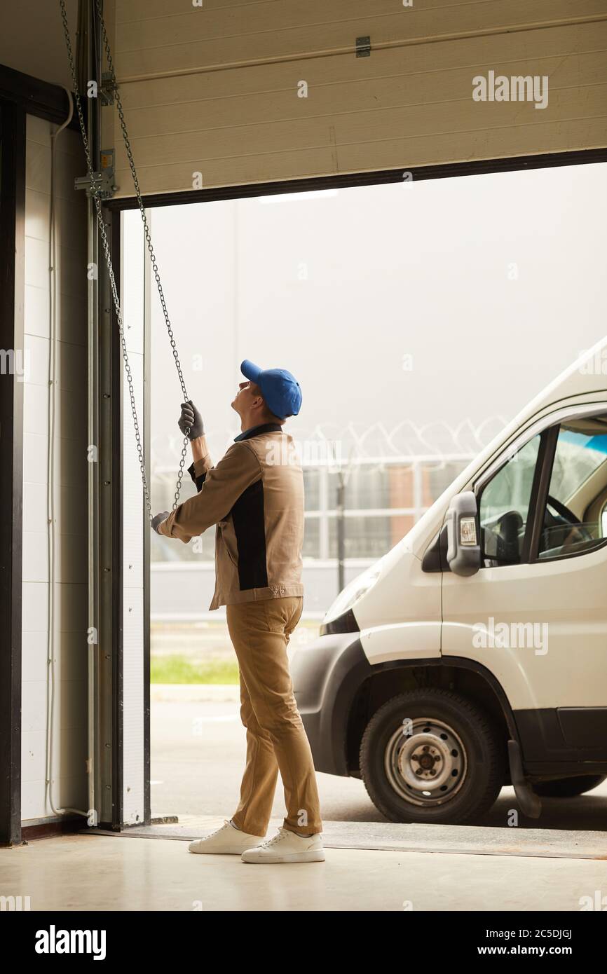 Manual worker in uniform opening the garage for the van he working in ...