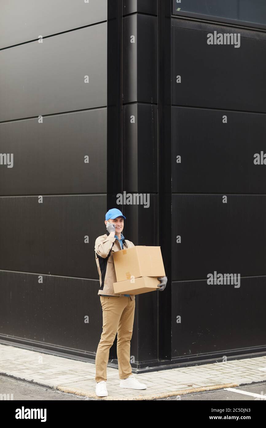 Young delivery person in uniform carrying boxes and talking on mobile ...