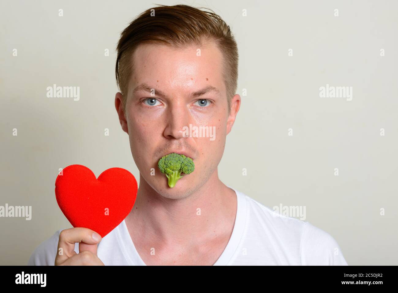 Portrait of young handsome man eating broccoli and holding heart Stock ...