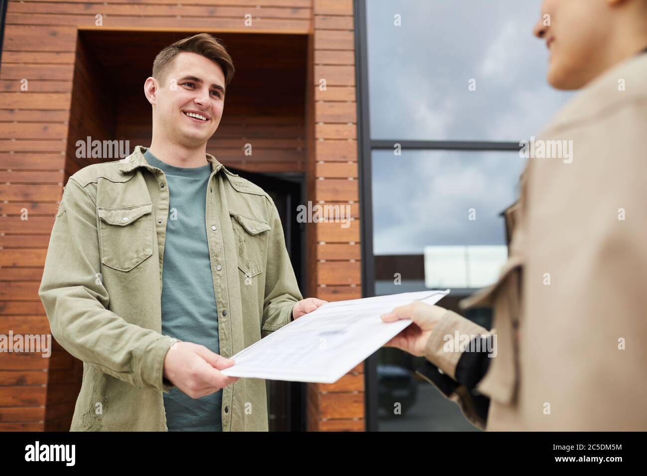 Young smiling man getting the letter from postman while they standing ...