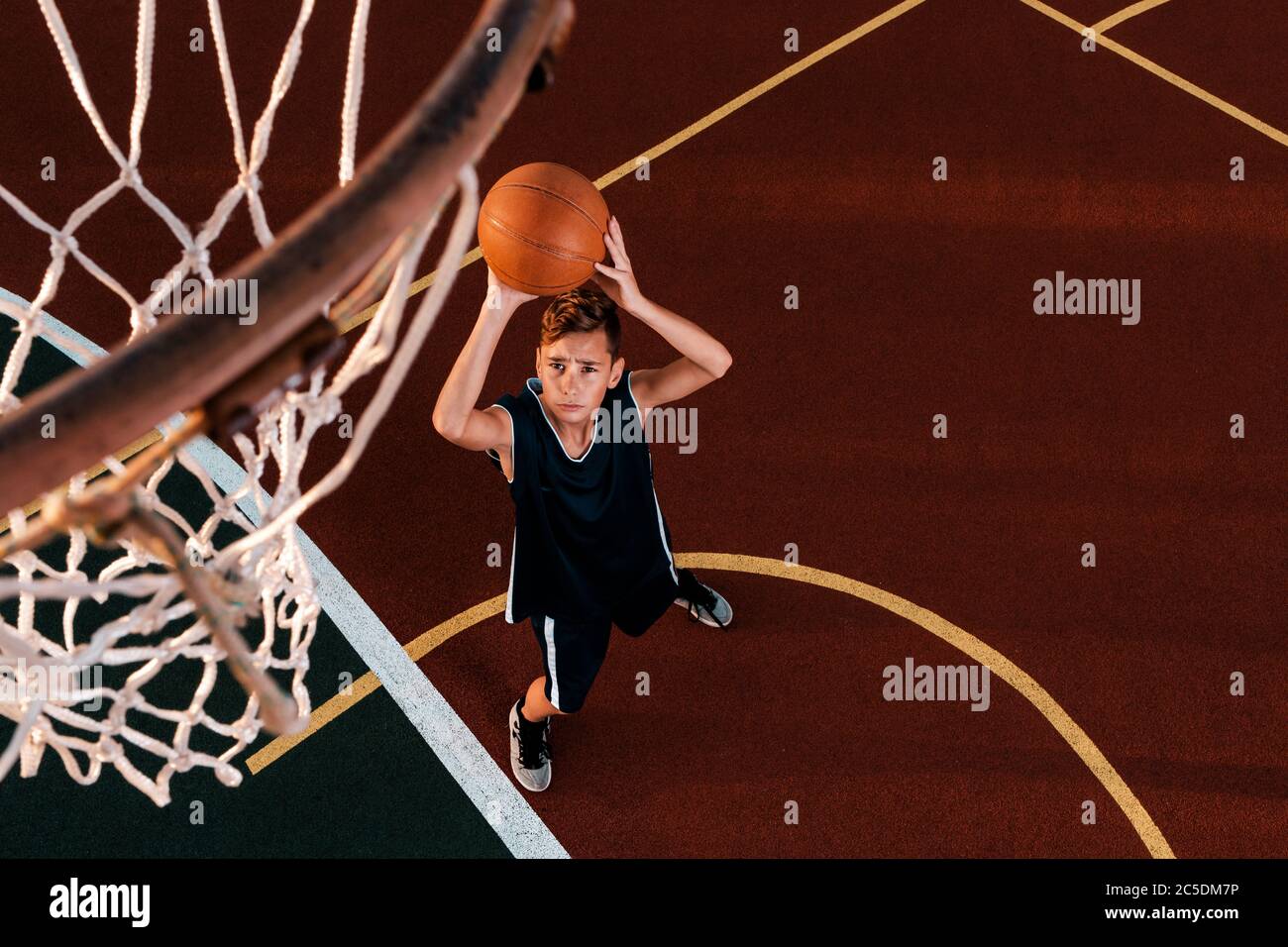 A young teenager in a tracksuit throws a basketball into the basket ...