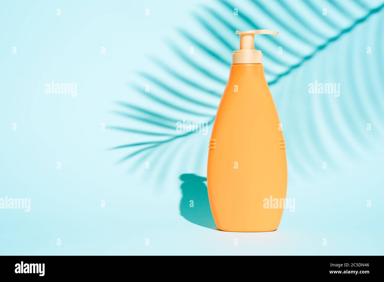 Orange container for lotion without label on blue background with leaf ...