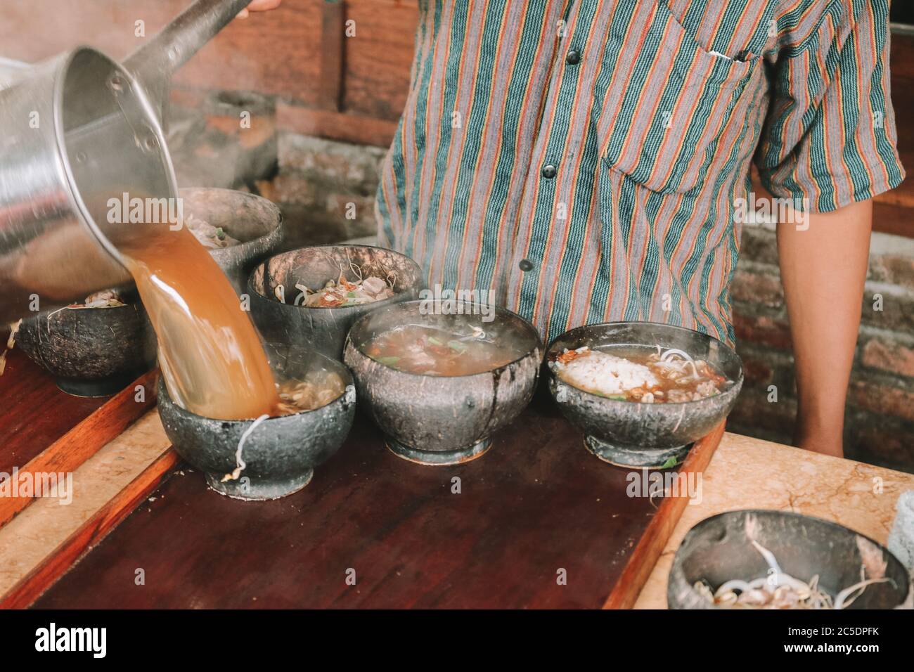Chef using Lurik uniform pouring a soup into soto bathok in Yogyakarta ...