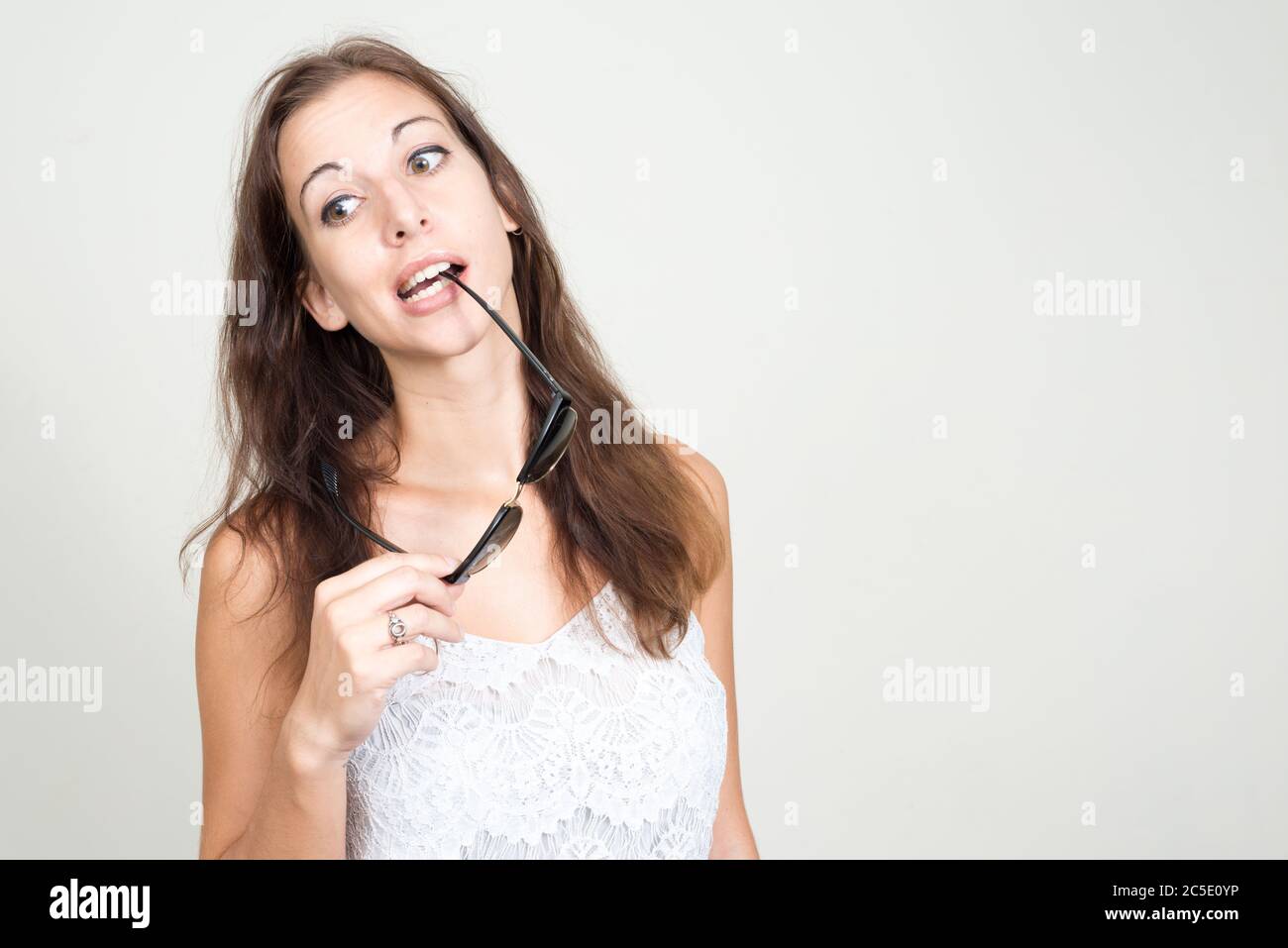 Portrait of young beautiful woman biting sunglasses Stock Photo - Alamy