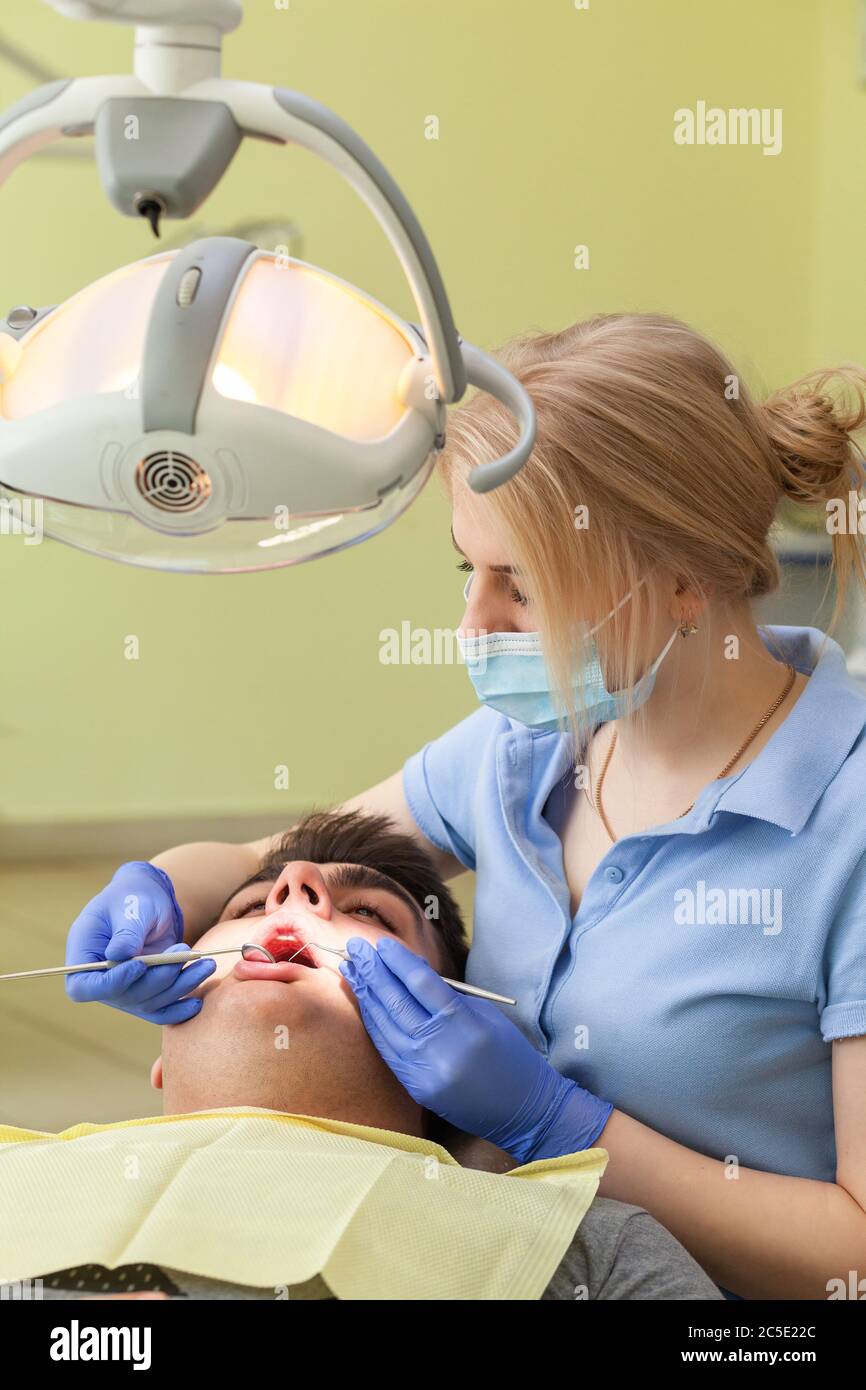 Man visiting female dentist at clinic. Young man sitting mouth wide ...