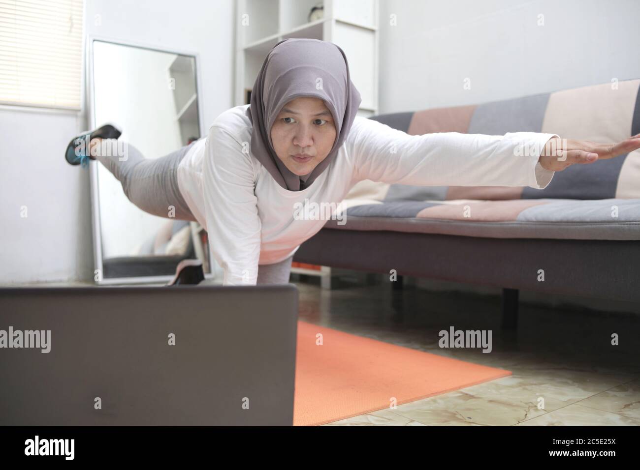 Asian muslim woman wearing hijab doing exercise at home while watching ...