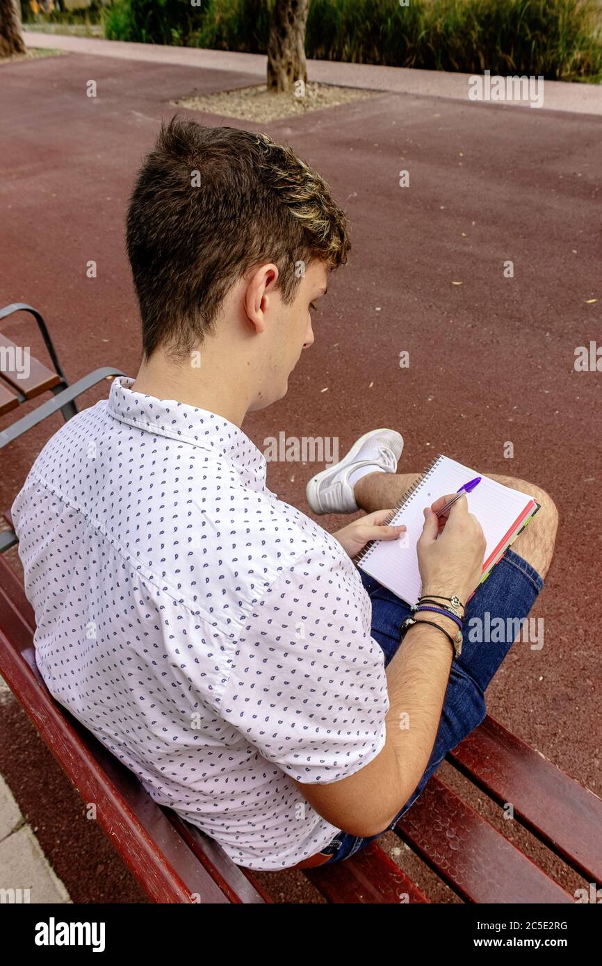 Young man sitting on bench writing on notepad hi-res stock photography ...