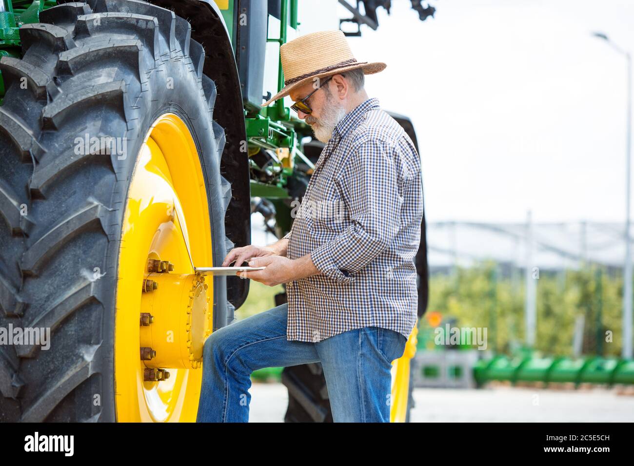 Professional farmer with a modern tractor at work with laptop. Looks ...