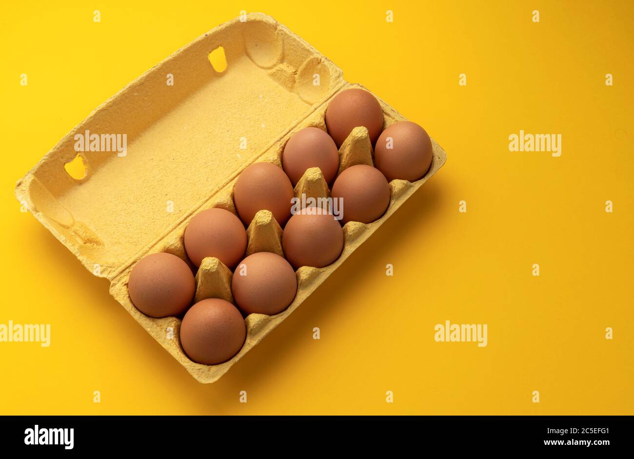 Brown chicken eggs in cardboard box on yellow background, top view ...
