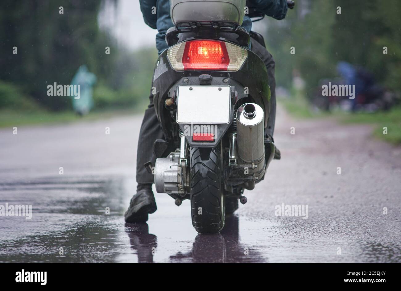 Motorcycle moped rides through a puddle on a wet road in the rain ...