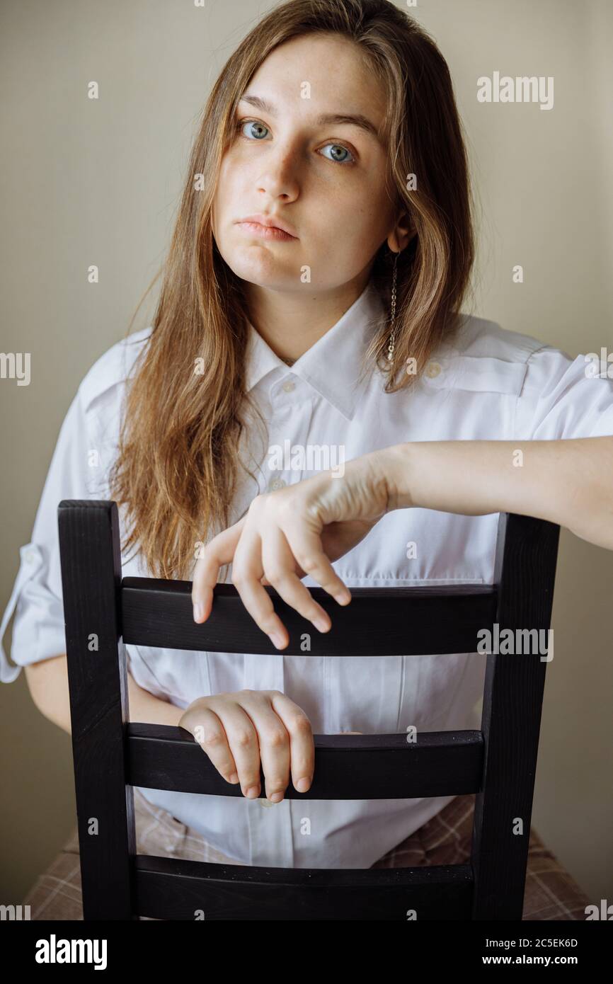 A brunette girl without makeup with her hair down is sitting on a chair ...