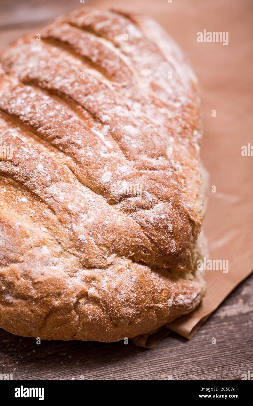 Crusty bloomer loaf, unwrapped from brown paper wrapping, over old wood ...