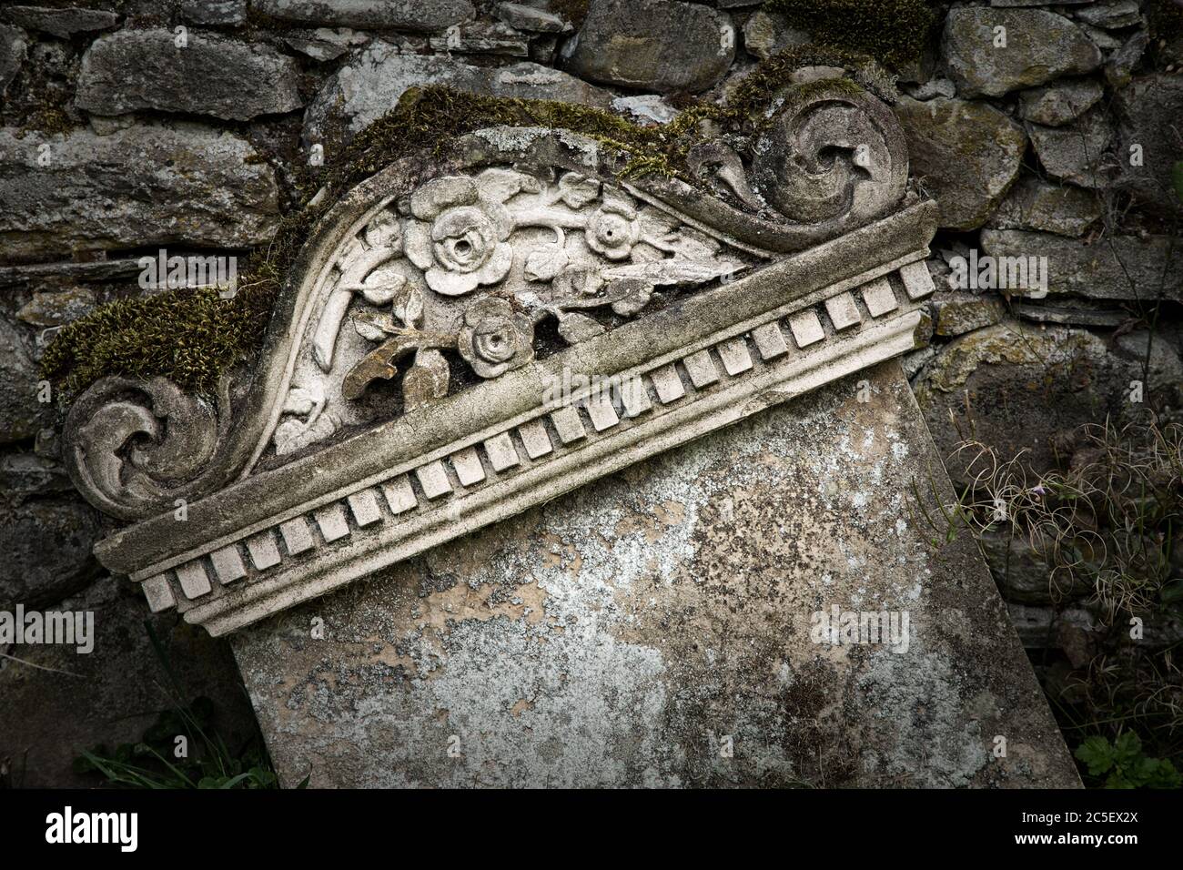 Neglected old gravestone against old stone wall. Intentional vignette ...