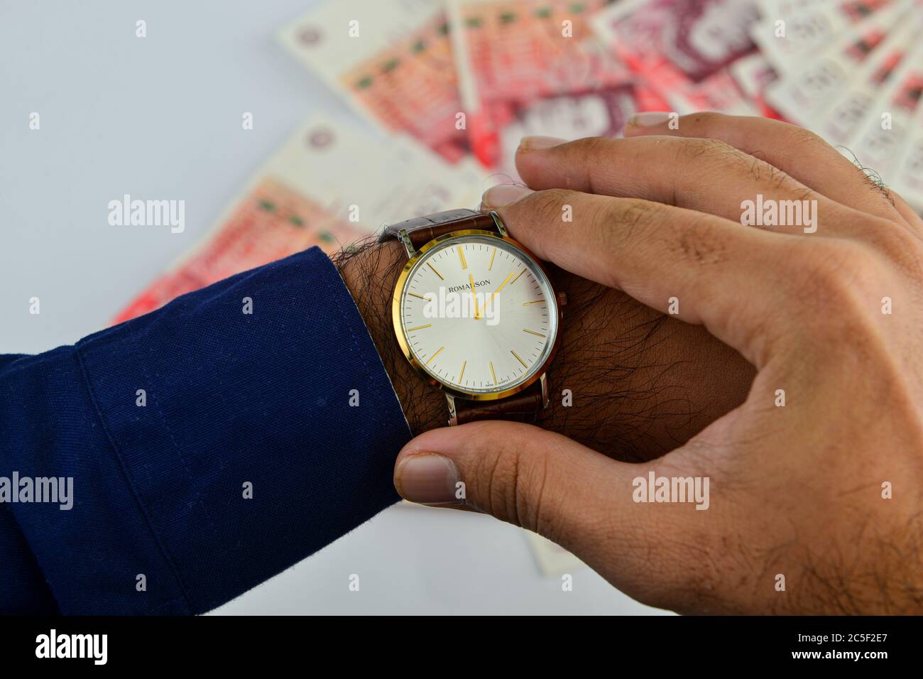 Wrist watch on man's hand in front of a British Currency and white ...