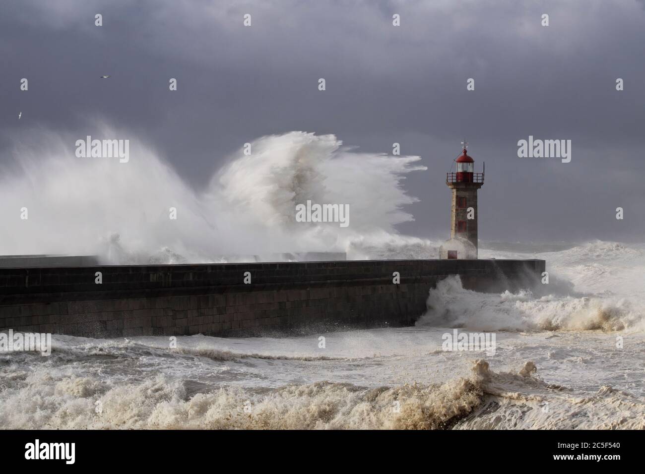 Big white waves over piers and lighthouse against a stormy dark cloudy ...