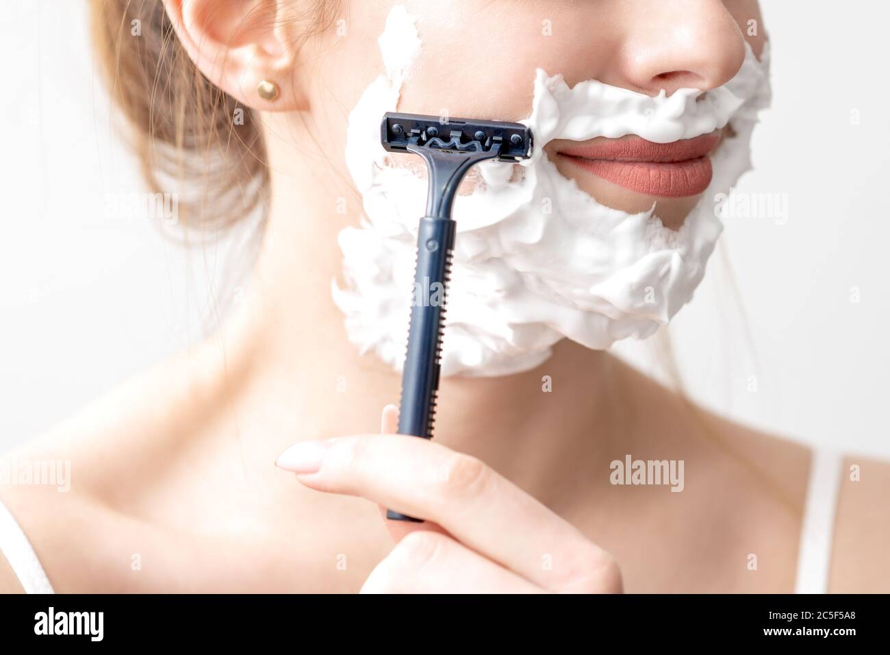 Beautiful young caucasian woman shaving her face by razor on white ...