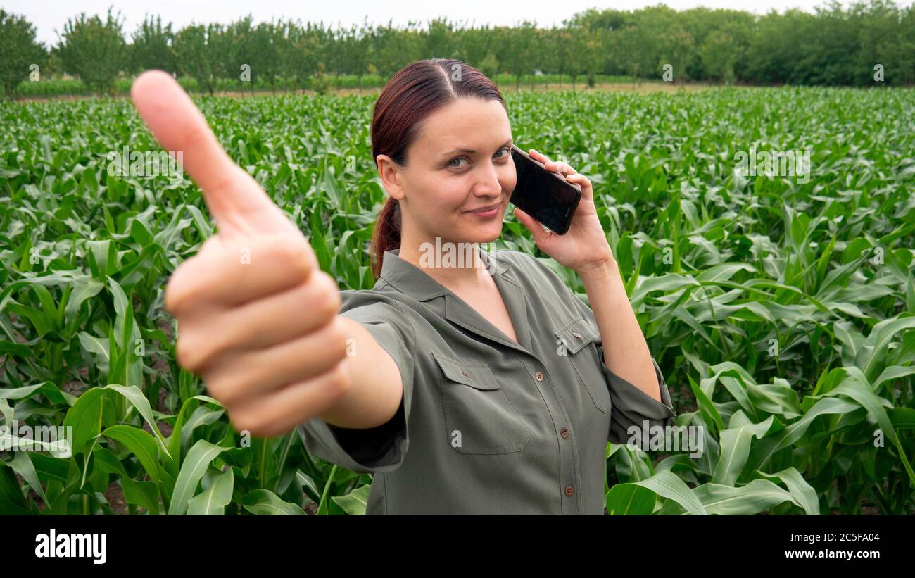 Smiling female farmer on phone looking at the camera in corn field ...