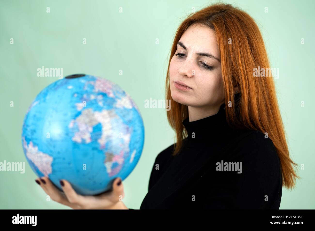 Portrait of a sad worried young woman holding geographic globe of the ...