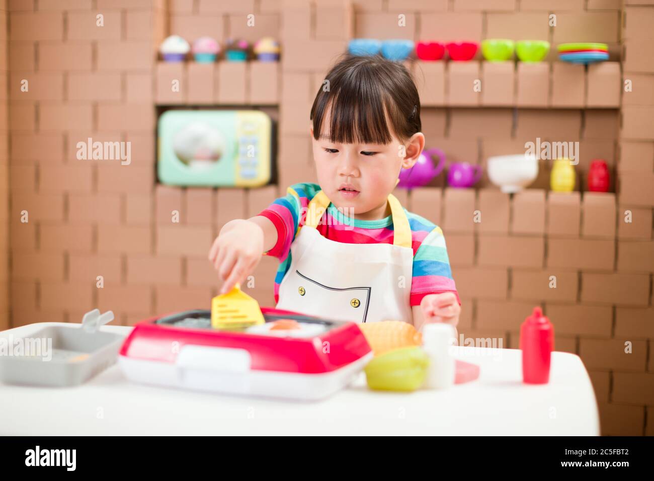 toddler girl pretend play food preparing role against cardboard blocks ...
