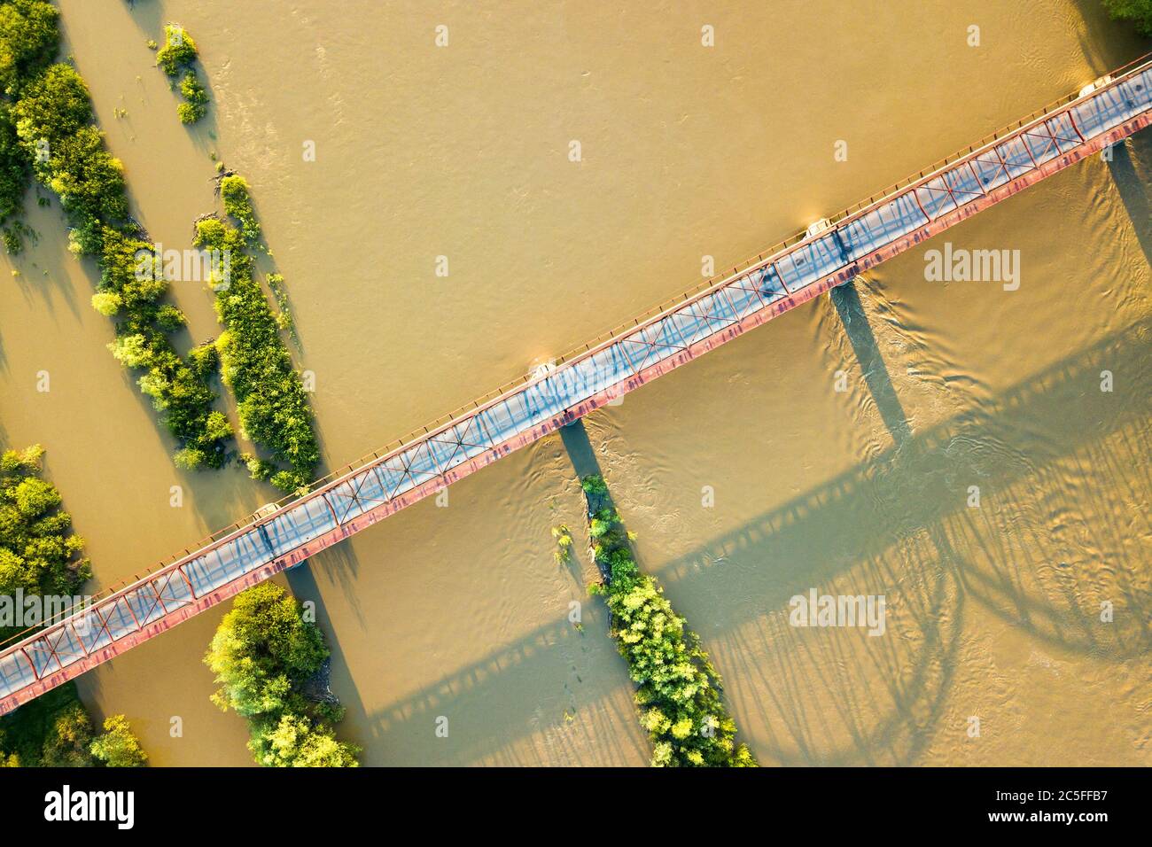Aerial view of a narrow road bridge stretching over muddy wide river in ...
