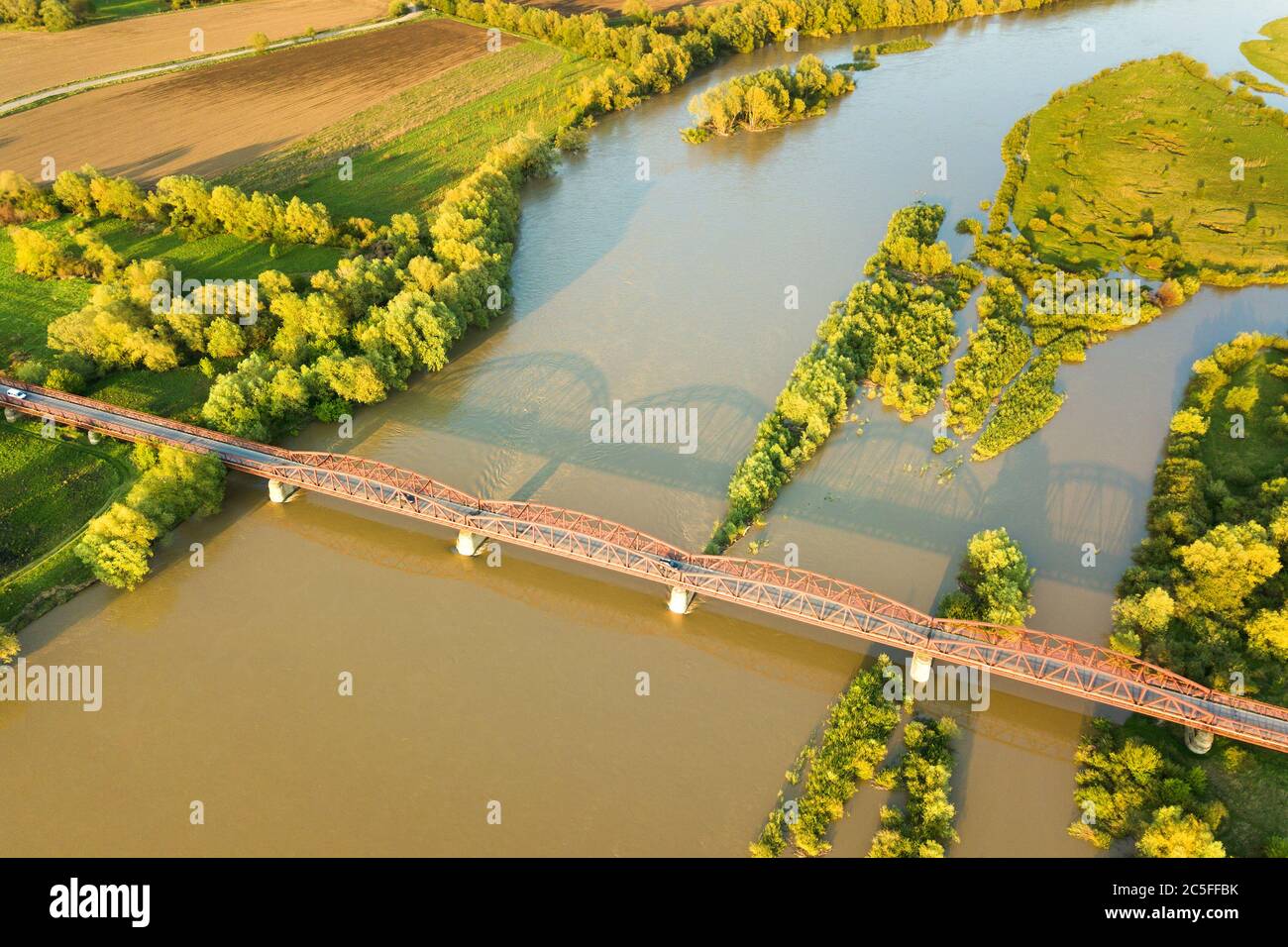 Aerial view of a narrow road bridge stretching over muddy wide river in ...