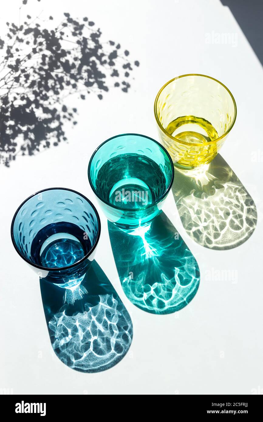 Colored glass cups filled with water with small flowers under the ...