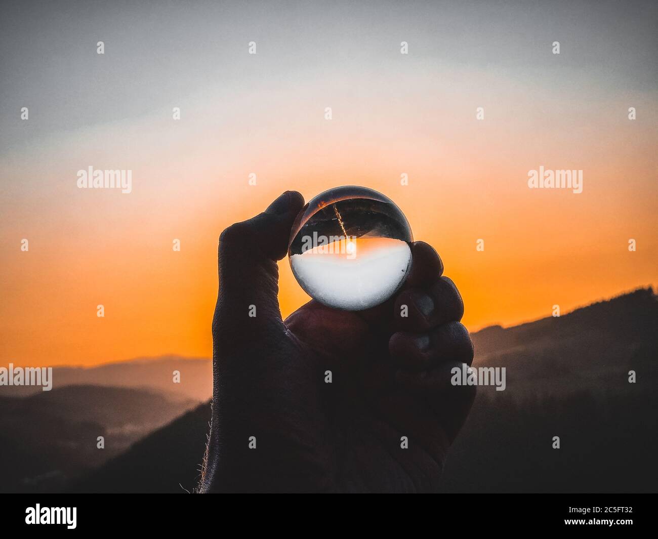 Taking photos of sunset through the small glass ball holding in hand ...