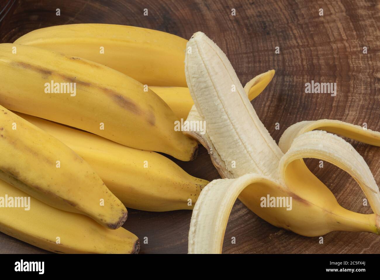 close up of peeled banana, bunch of bananas at the bottom of a wooden ...