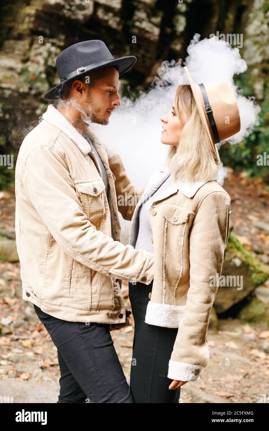 Couple in vape cloud. Two in smoke. Tourists in cold autumn forest with ...