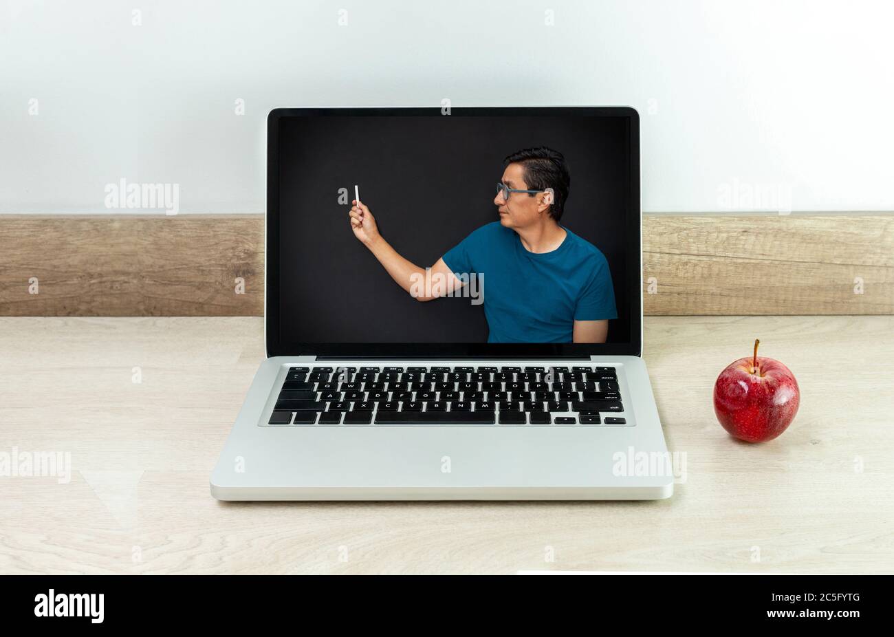 On a desk a laptop shows a teacher giving virtual classes pointing with ...