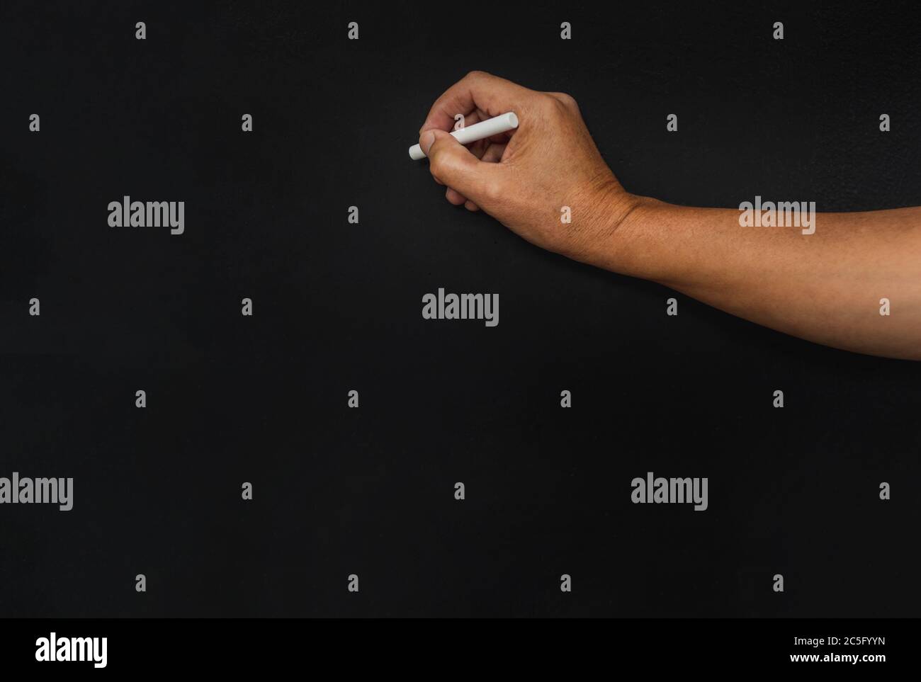 Black chalkboard with a hand that has a chalk to write or draw on it ...