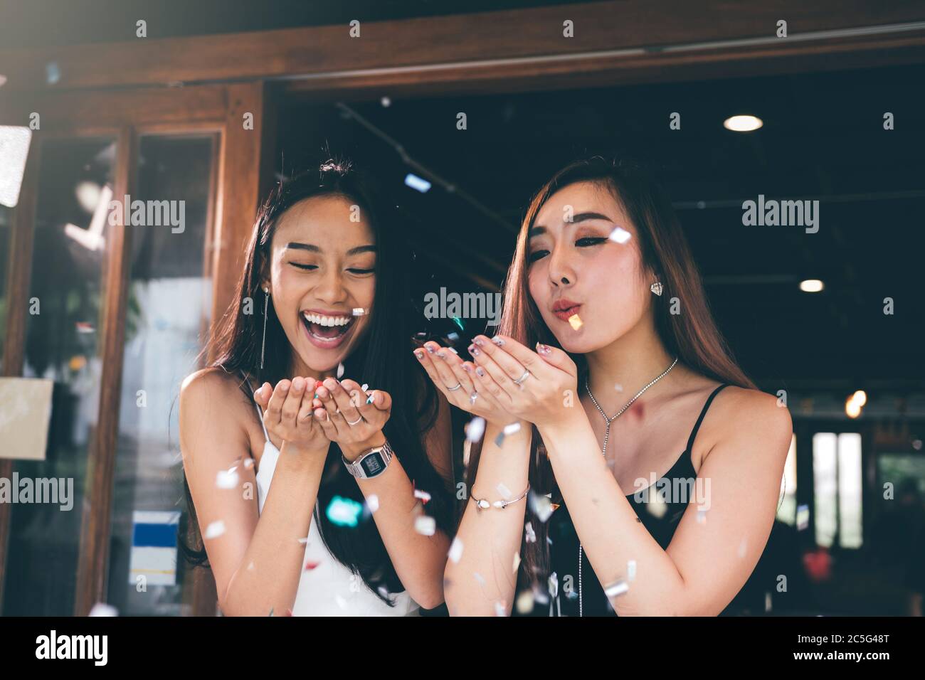 Two asian women blowing paper confetti for a celebration in his home ...