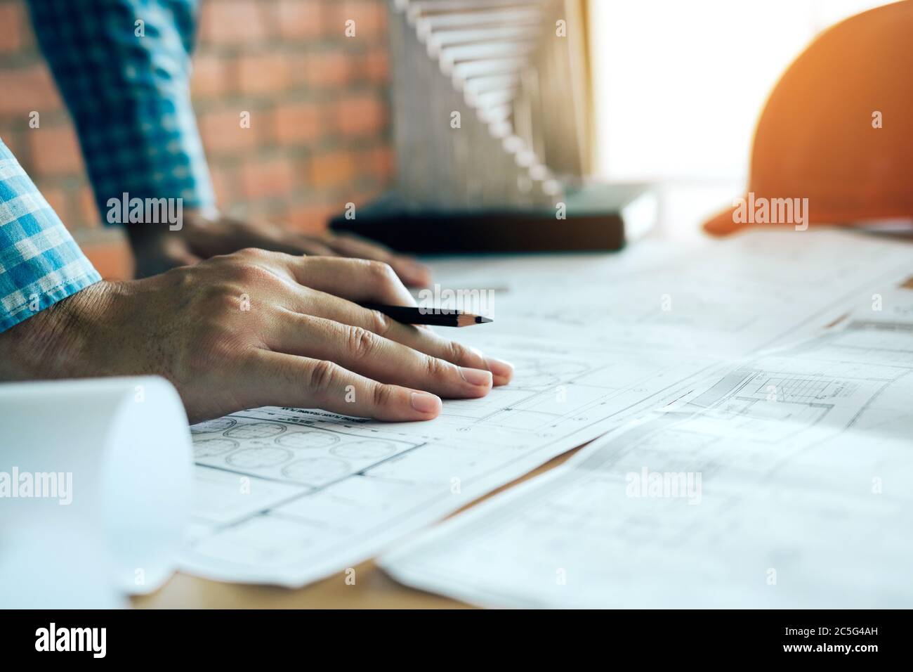 Hand of young engineering man drawing on blueprint with model on desk ...