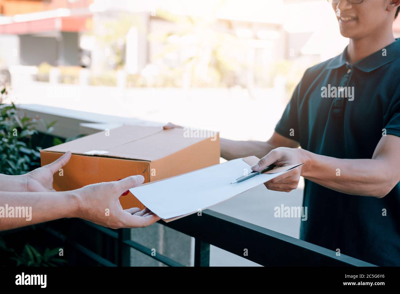 Young asian man smiling while delivering a cardboard box to the woman ...