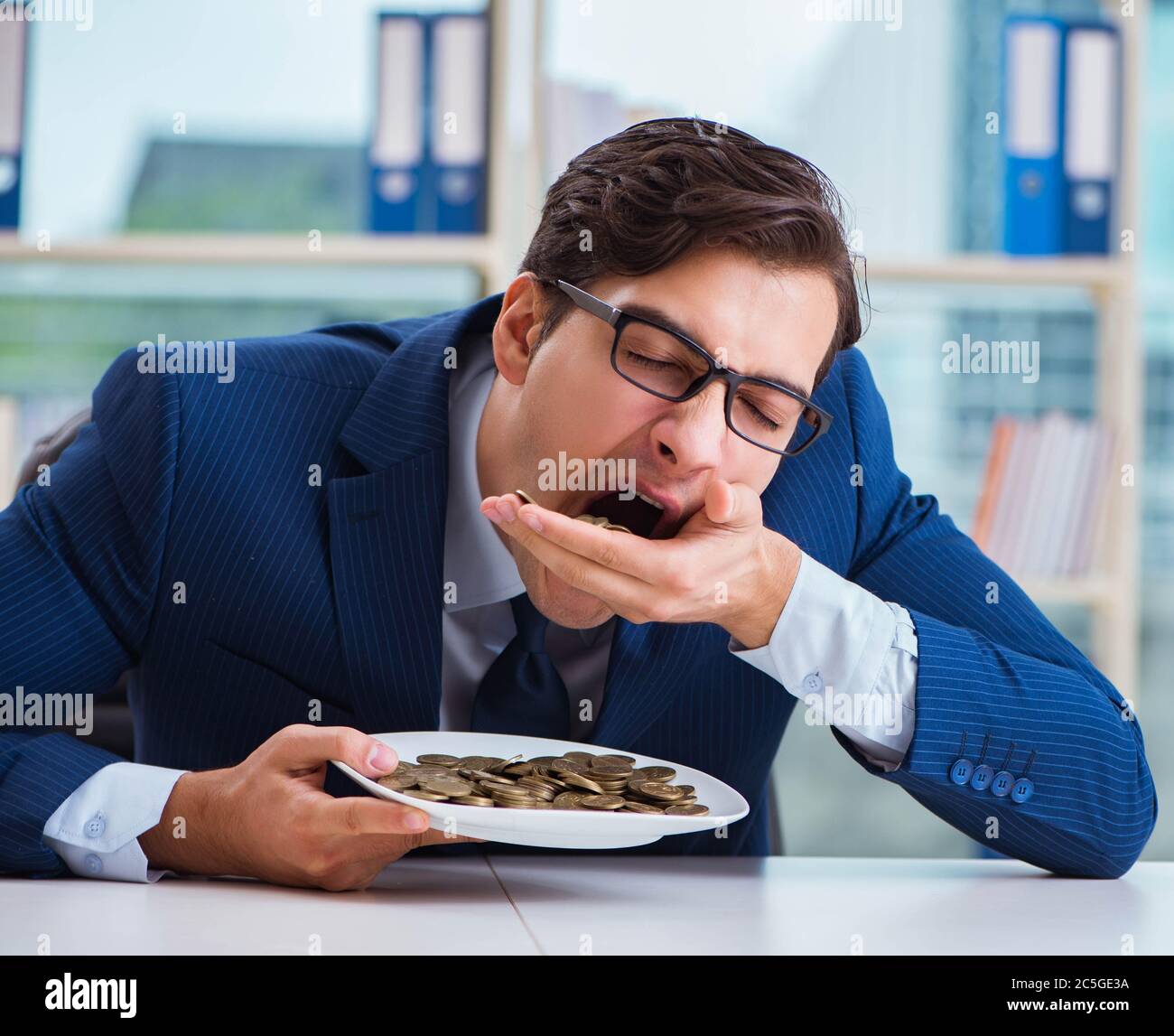 The funny businessman eating gold coins in office Stock Photo - Alamy